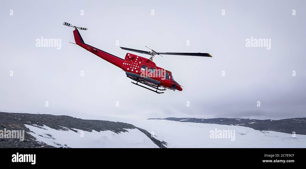 Red helicopter in flight low over snow covered mountain Stock Photo - Alamy