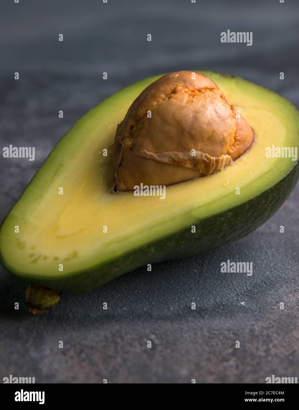 Flat lay photoshot of halved green avocado with a stone on the grey ...