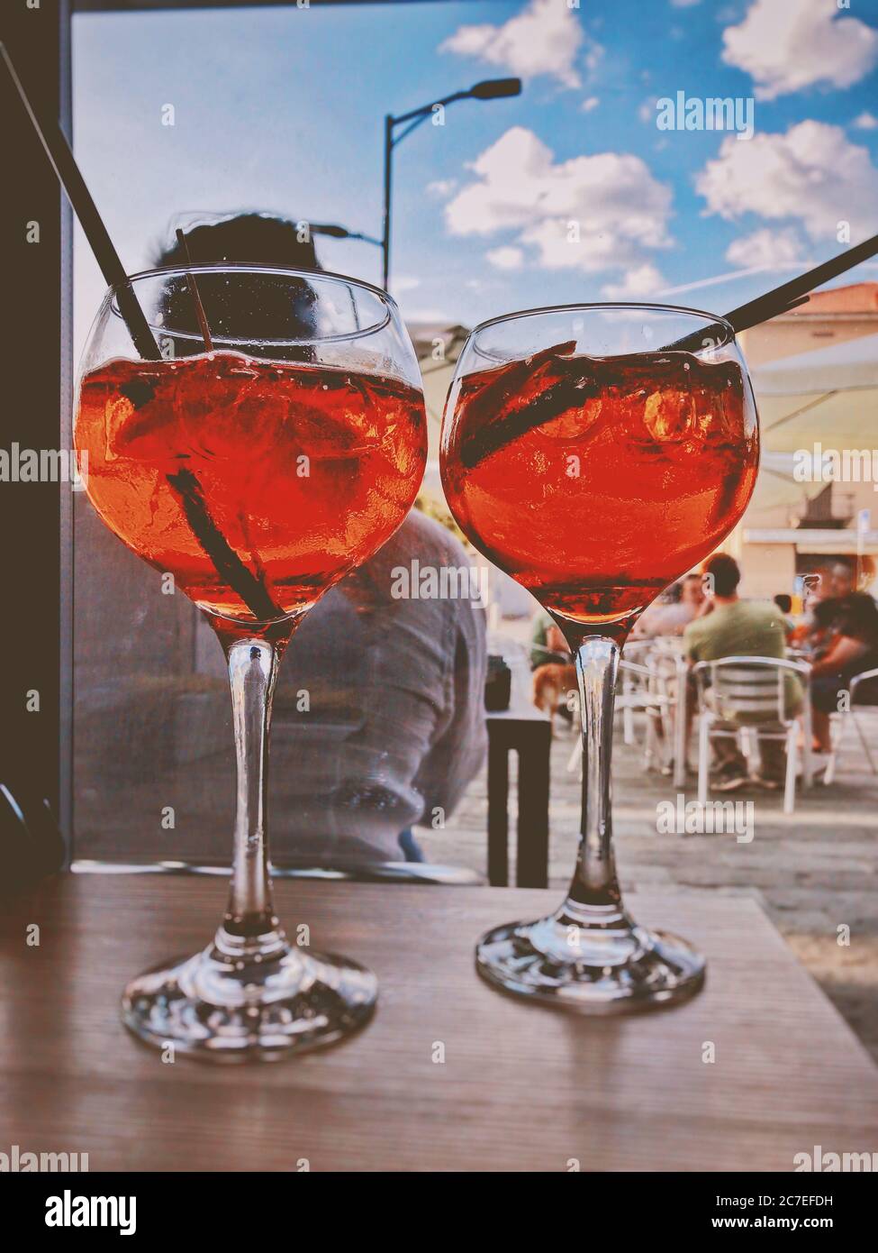 Vertical shot of two glasses of red cocktail with straws on a wooden ...