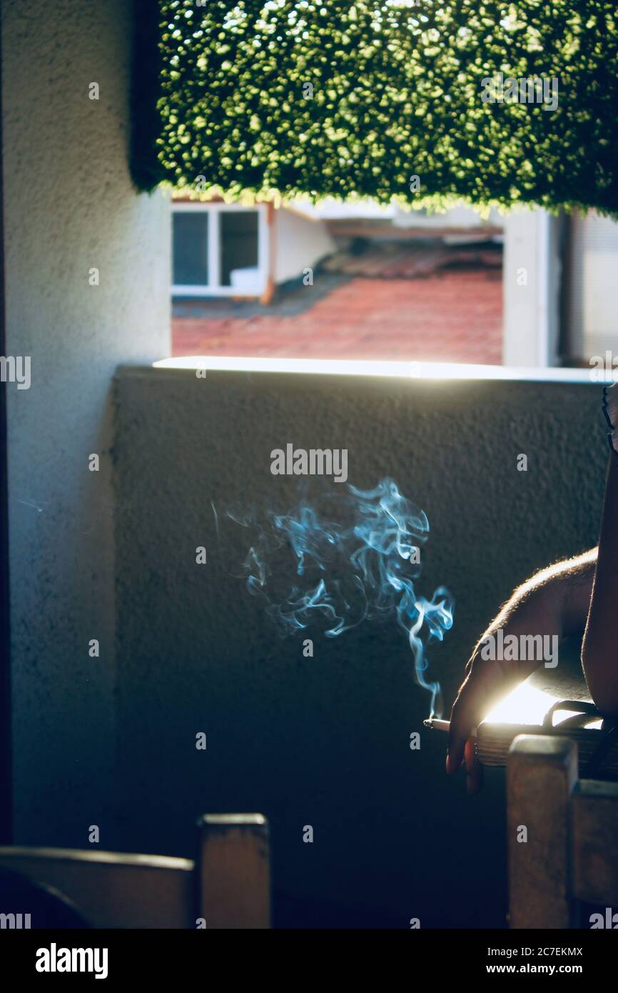 Vertical shot of a person smoking cigarette in a balcony with green ...