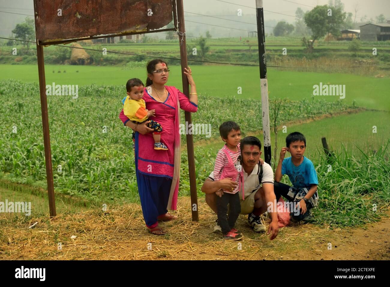 A rural family waiting for bus on the side of a road connecting Pokhara ...