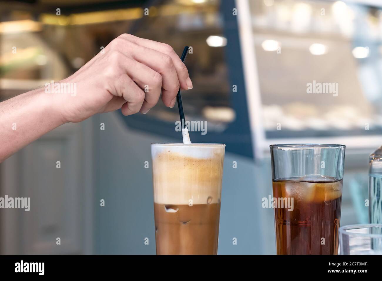 Female hand stirring a straw on a greek cold coffee, freddo cappuccino ...