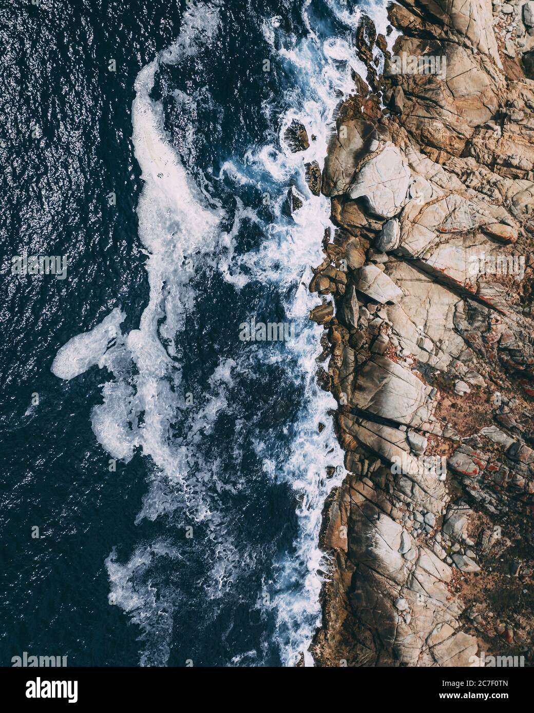 Vertical overhead shot of rocky shoreline next to a body of water with ...