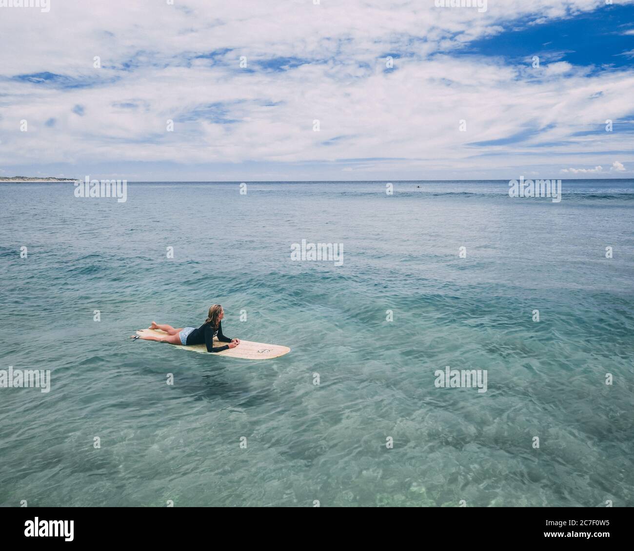 Horizontal Shot Of A Woman Lying On A Surfboard In A Body Of Water