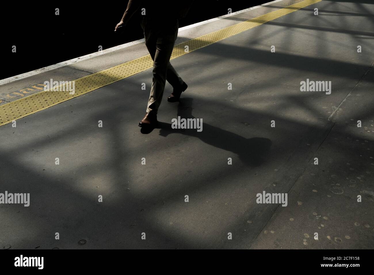 Horizontal shot of a male with his shadow walking on the road at ...