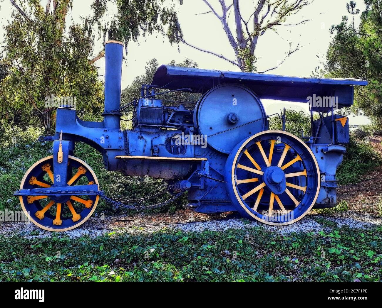 Blue vehicle with a steam engine near trees with a bright sky in the ...