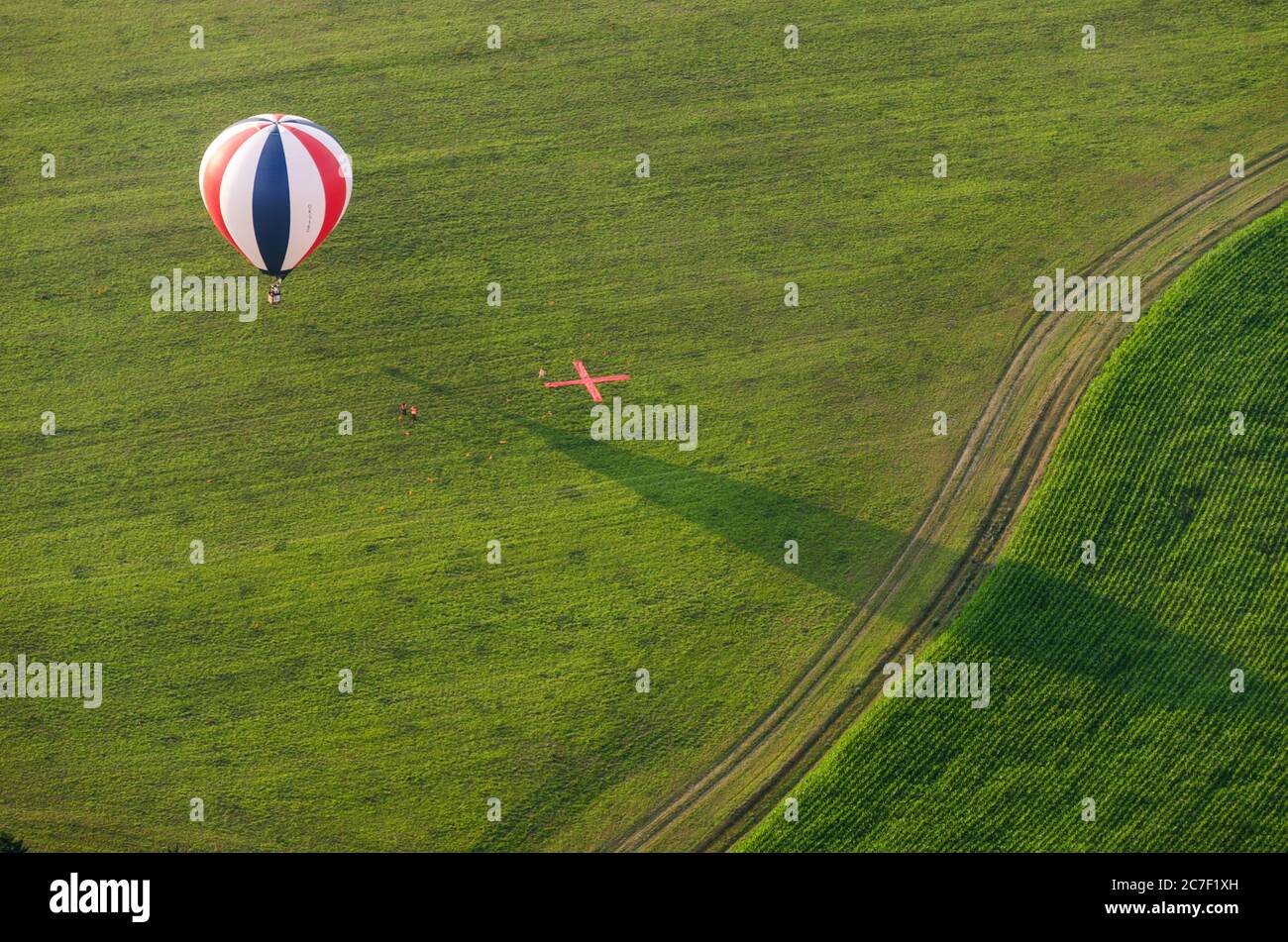 Aerial shot of a hot air balloon landing in a green grass field with ...