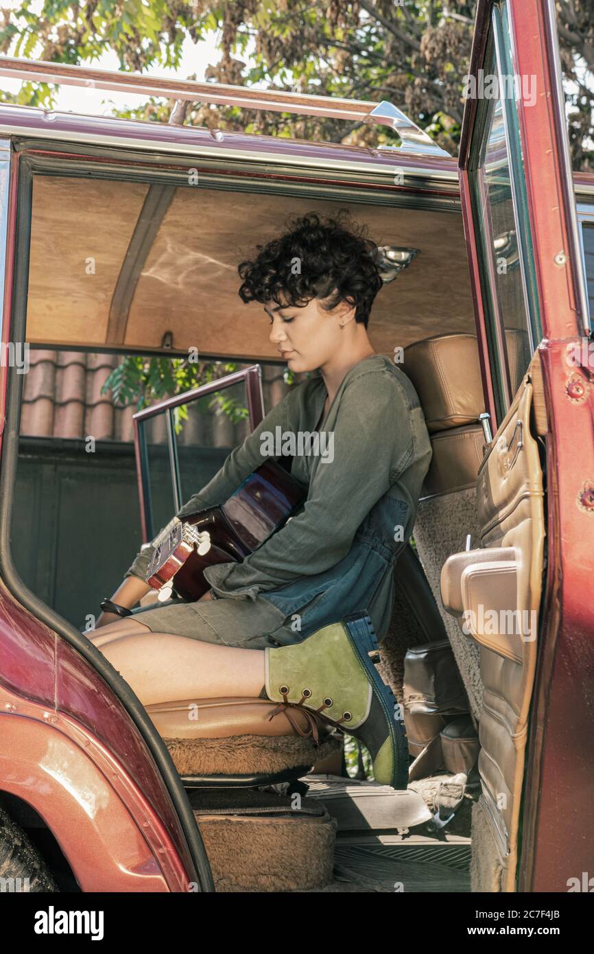 Curly model sitting in a car with a guitar posing for a photoshoot ...