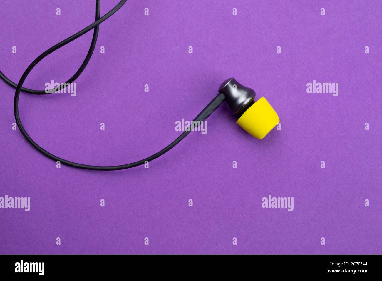 Earphone with yellow ear cushion on a purple background. in-ear ...