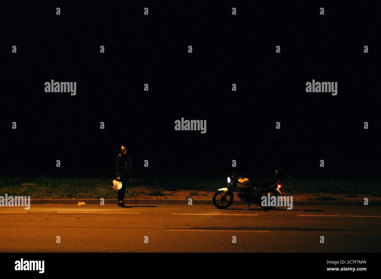 Biker standing near his motorcycle by the road at night with complete ...