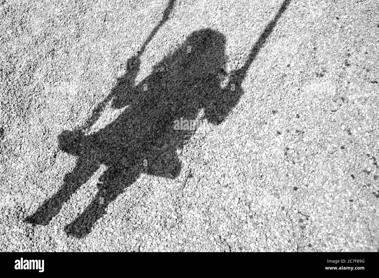 Shadow on the ground with stones of a kid on a child swing under ...
