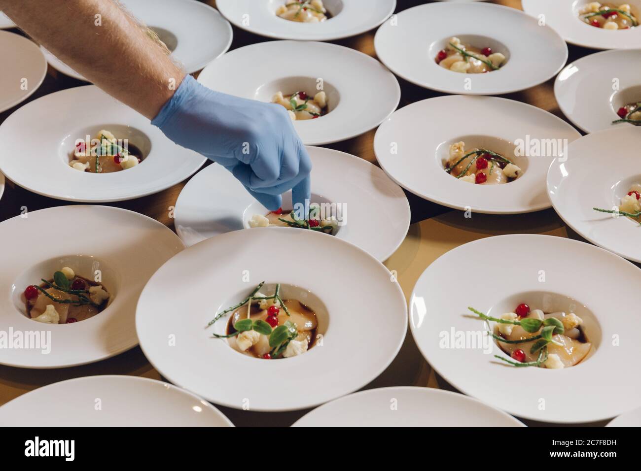 Cook adding ingredients on a dish filled in white serving plates in a ...