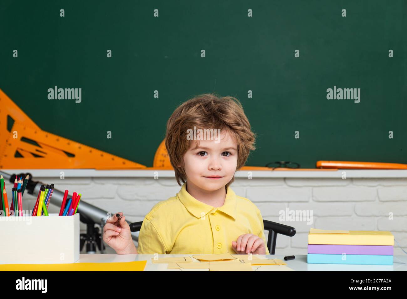 Happy cute industrious child is sitting at a desk indoors. Individual ...