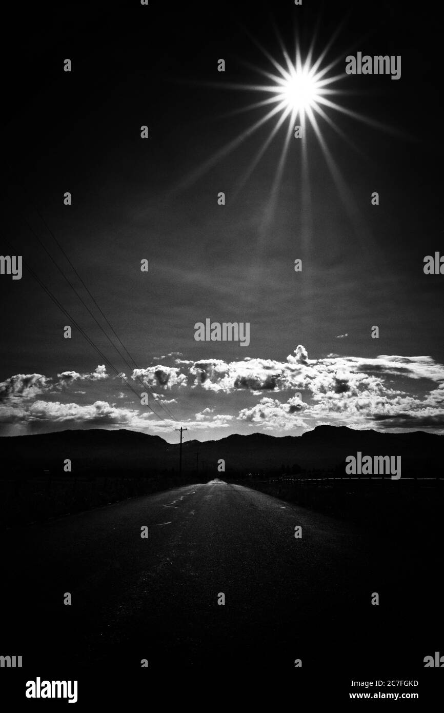 Vertical greyscale shot of the sun shining in the sky over an empty ...