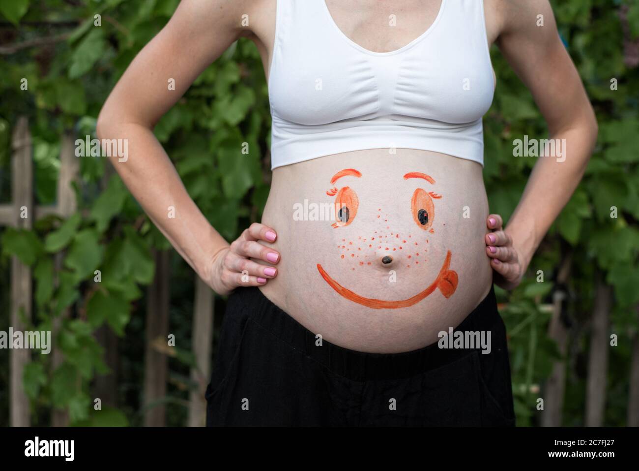 Belly of a pregnant woman with a painted smiling face. Green background ...