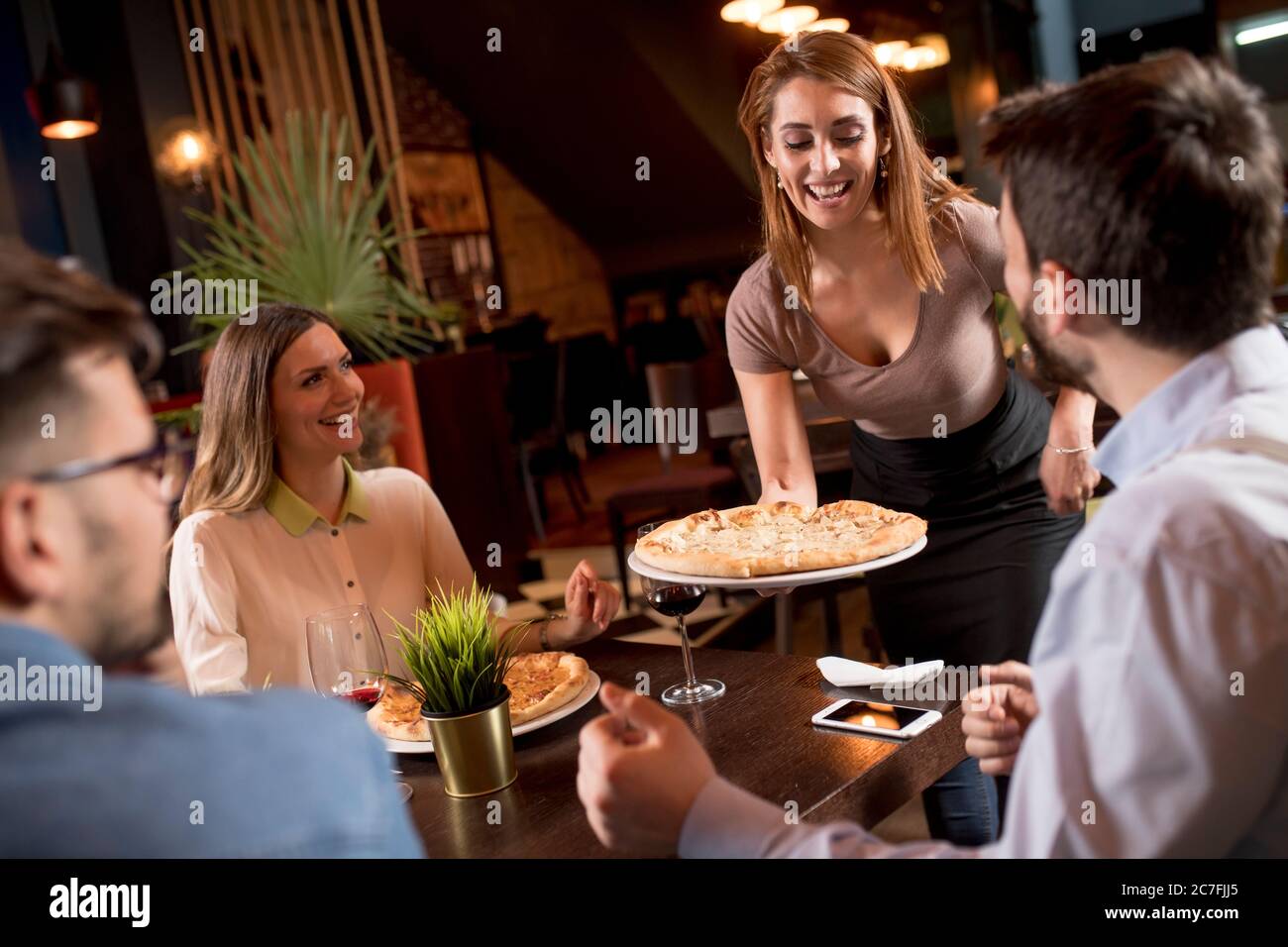 Pretty waiter woman serving group of friends with food in the ...