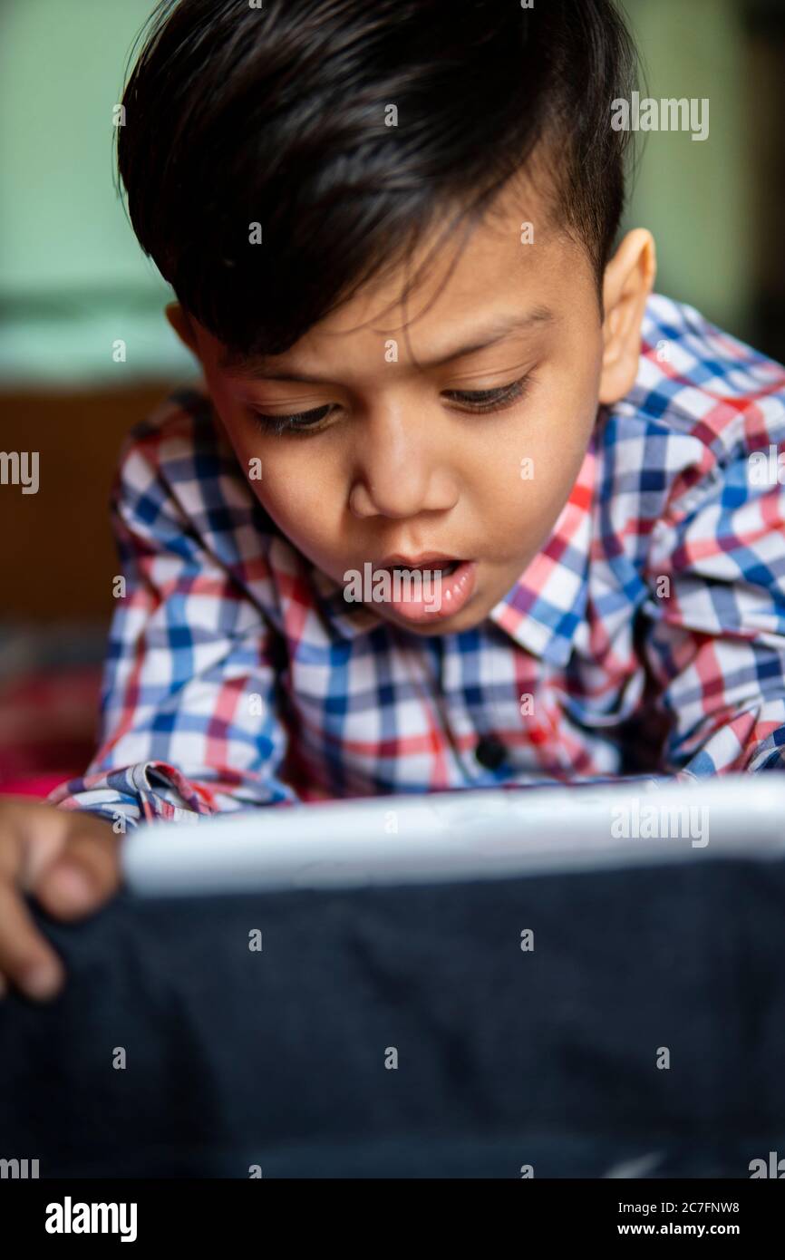 Indoor image of little boy lying on bed with hands on chin and watching ...