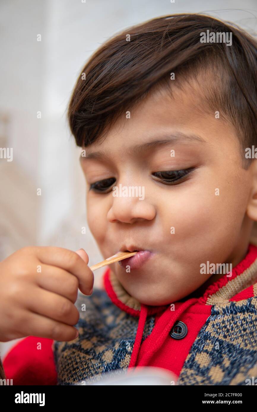 Close-up of cute little boy in red dress, eating cup ice cream with ...