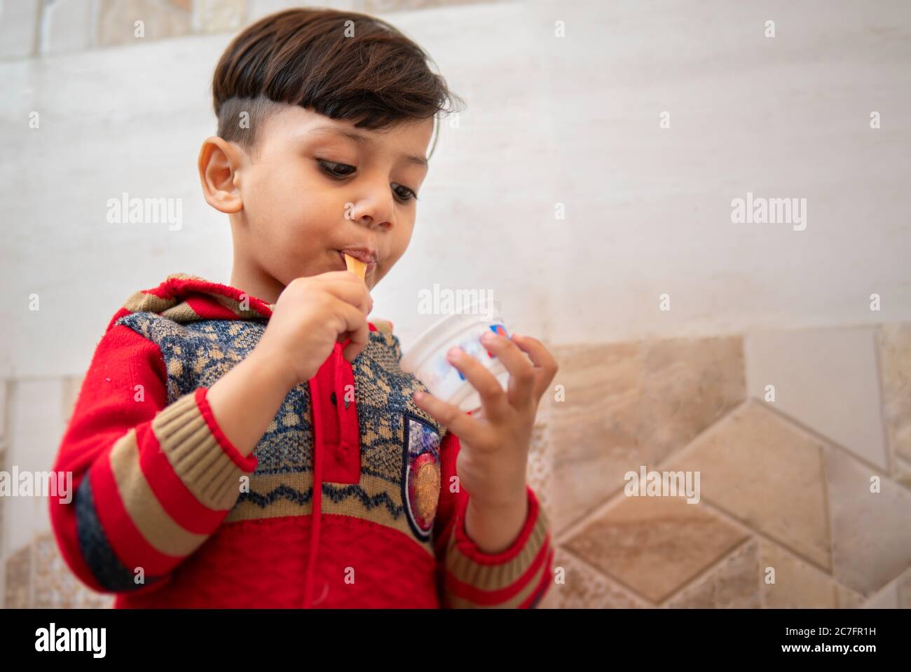 Low angle of cute little boy in red dress, eating cup ice cream with ...