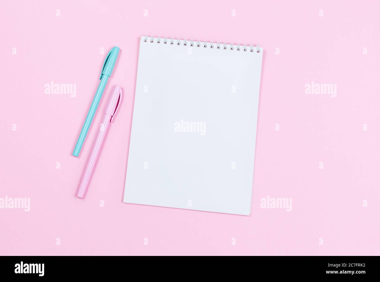 Notebook with blank page and two pens on a pink background. Flat lay ...