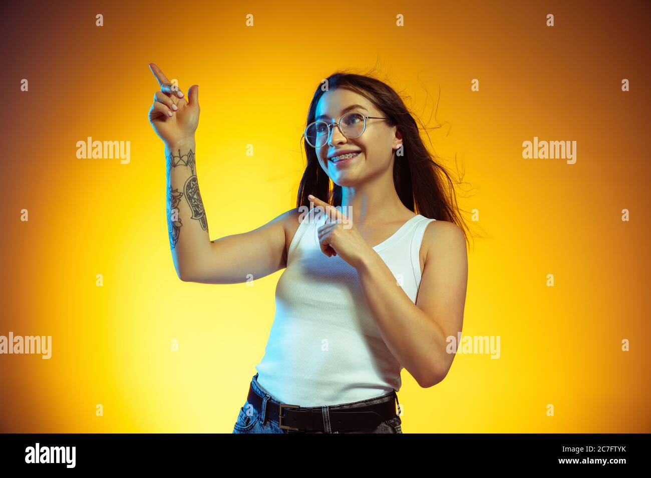 Pointing. Portrait of young caucasian woman isolated on gradient yellow ...