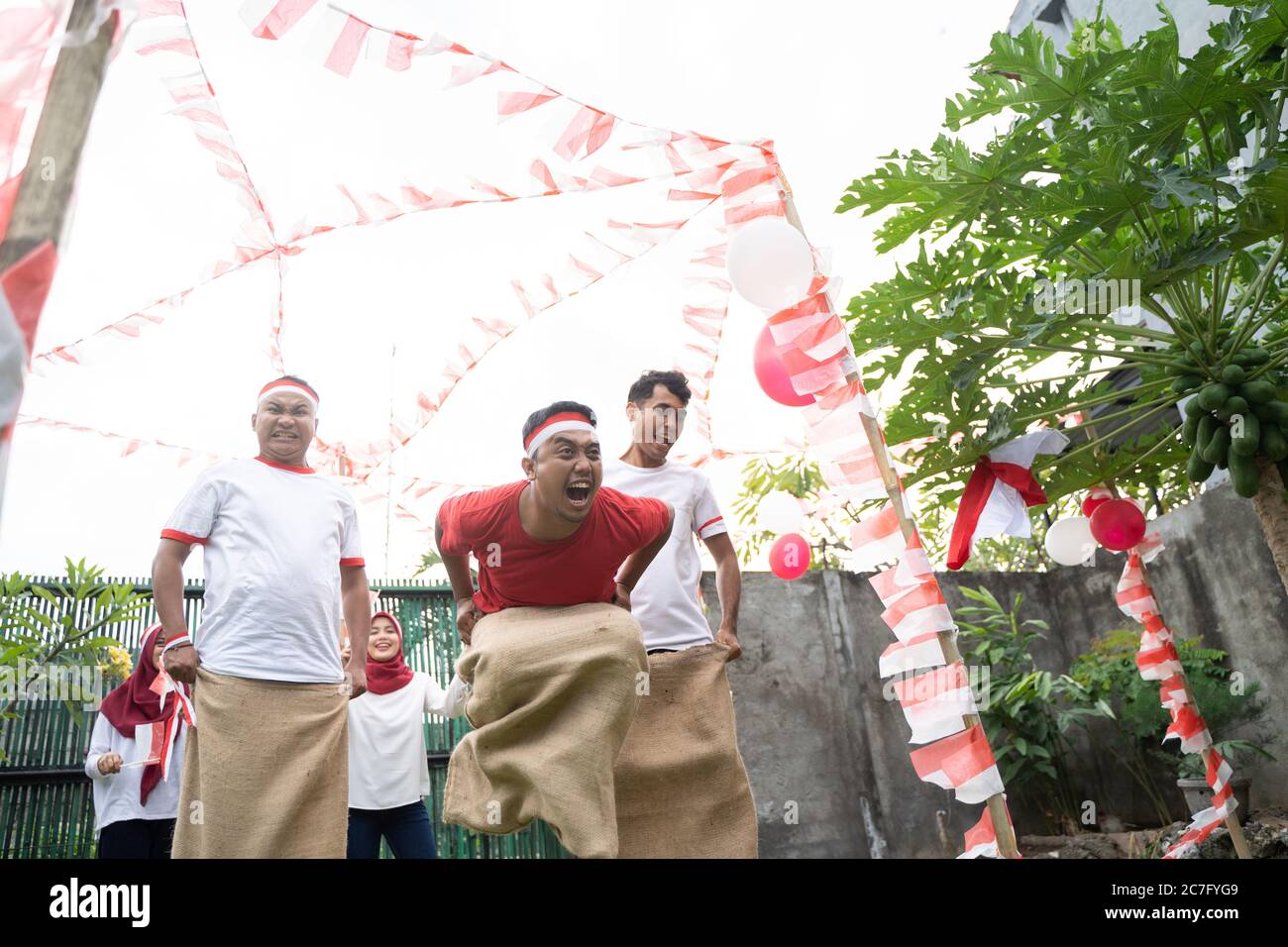 three young men happily joined in sack race jumping quickly to reach ...