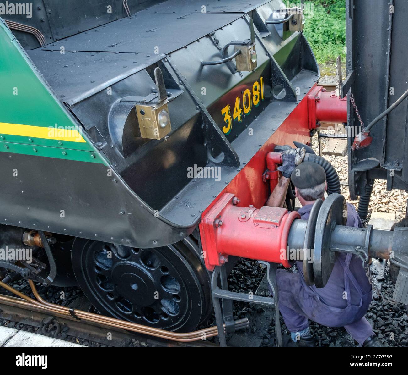 Steam engine driver seen crouching in front of his steam train, de ...