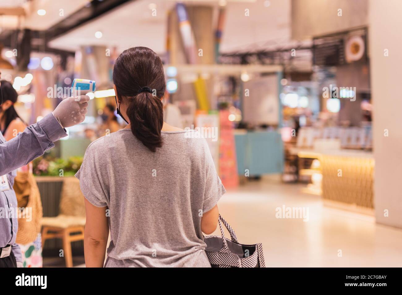 Security guard checking woman temperature at shopping mall entrance ...