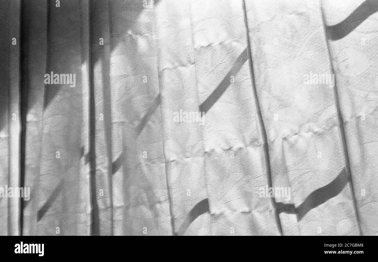 Grey scale shot of a white curtain on a window under the sun light ...