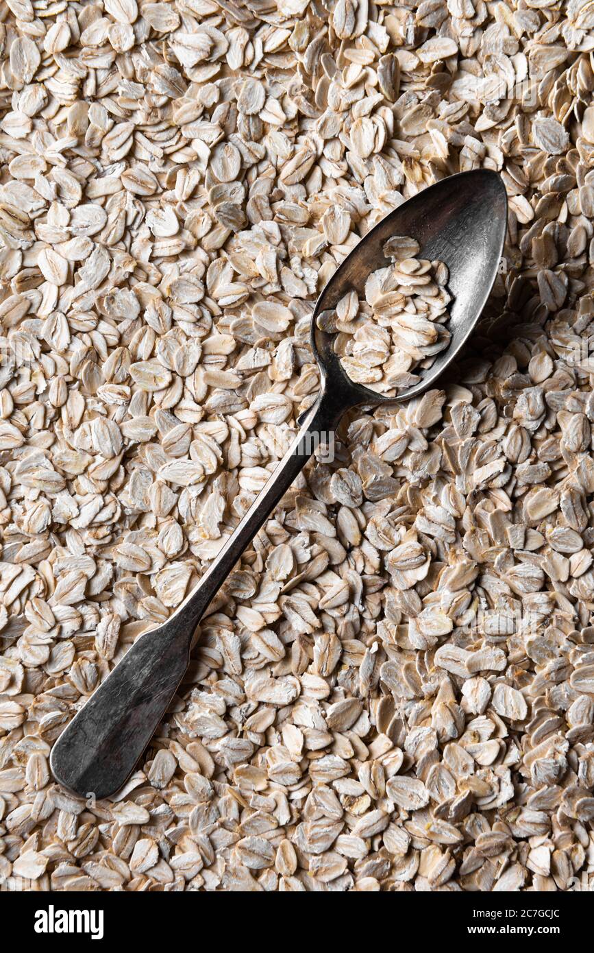 Metal spoon with few flakes of rolled oats in it. Spoon is on layer of ...
