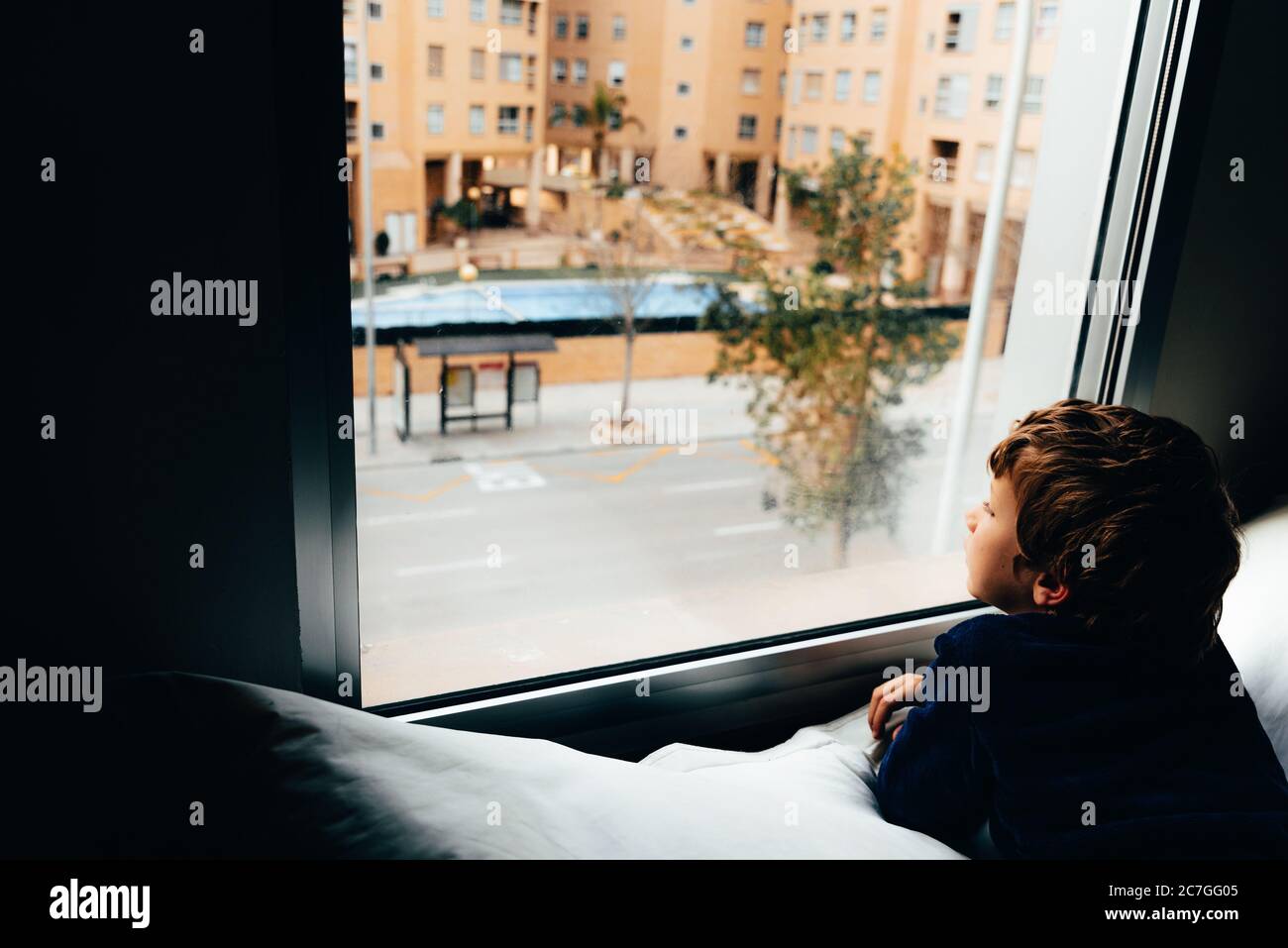 Sad and melancholic boy looks through a window in his apartment during ...