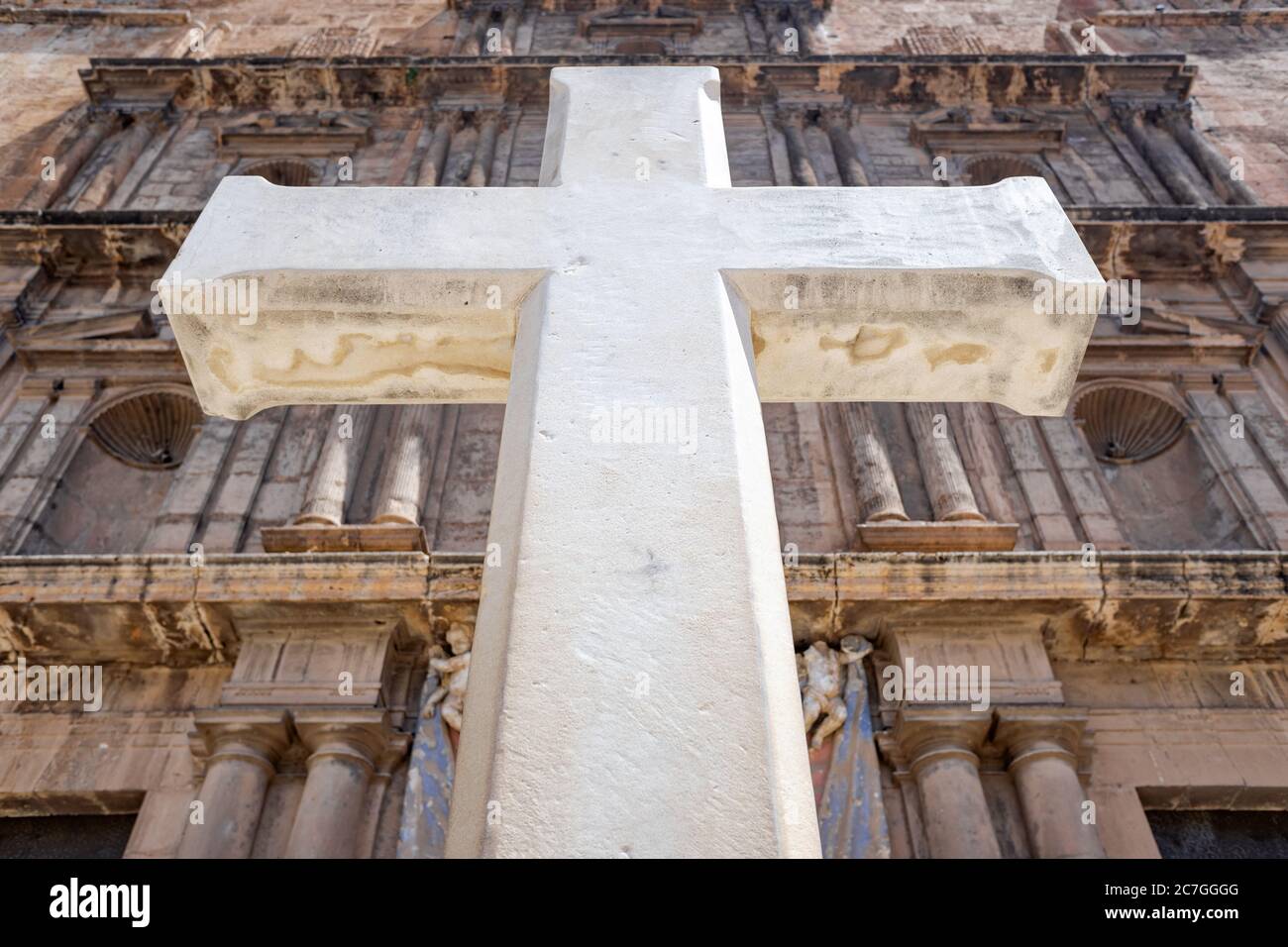 Cross carved in white stone, erected in front of a Christian religious ...