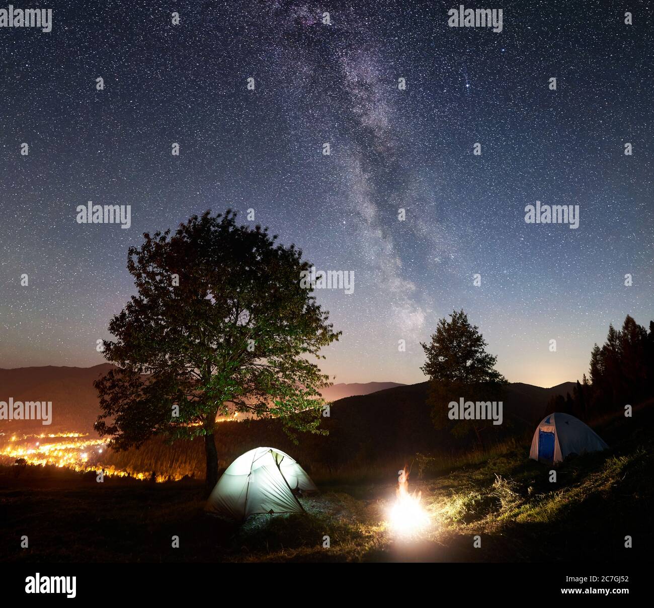 Tourist camping near big tree at night. Two tents and bonfire under ...