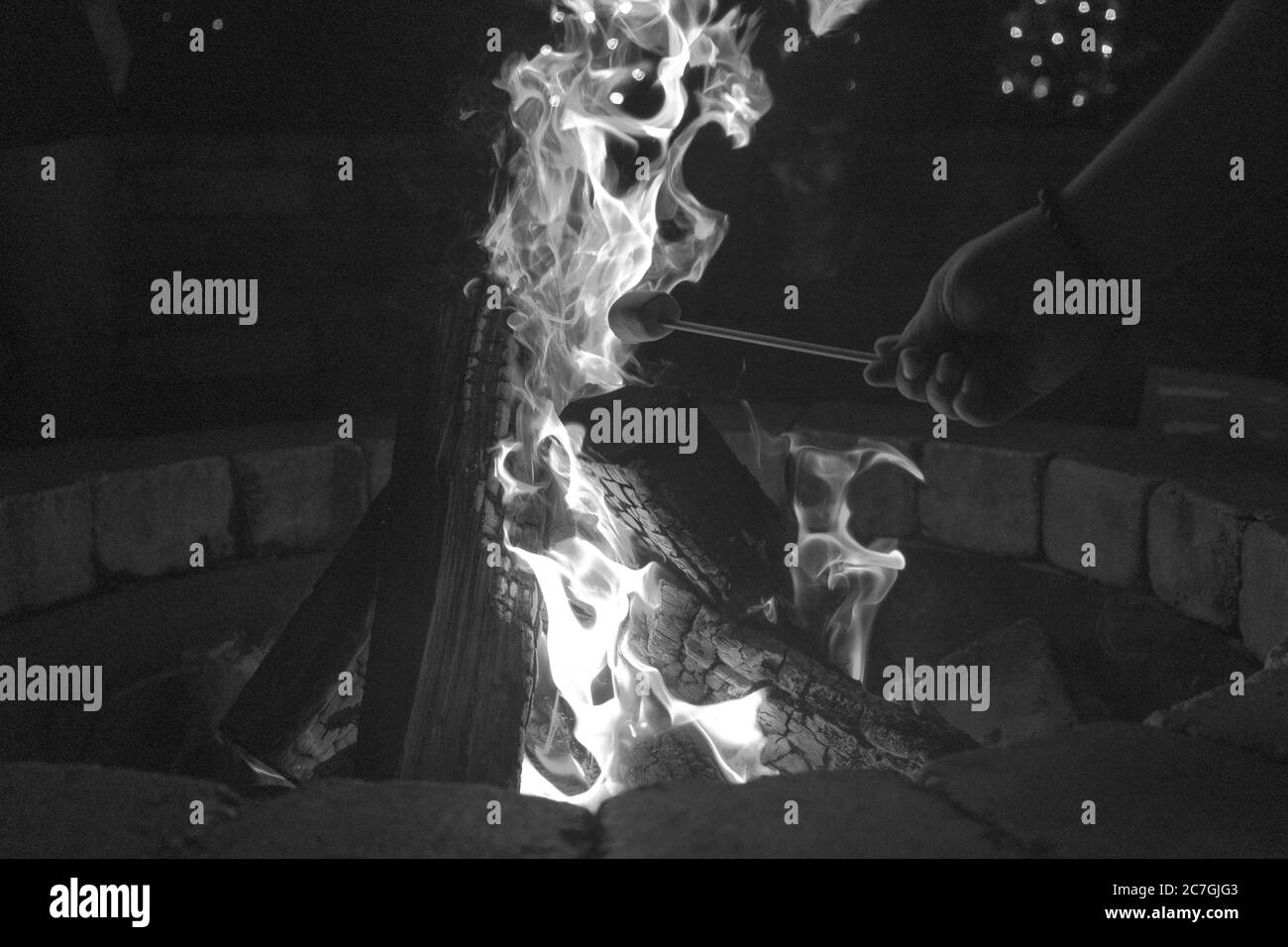 Grayscale closeup of a burning bonfire with a hand holding a ...