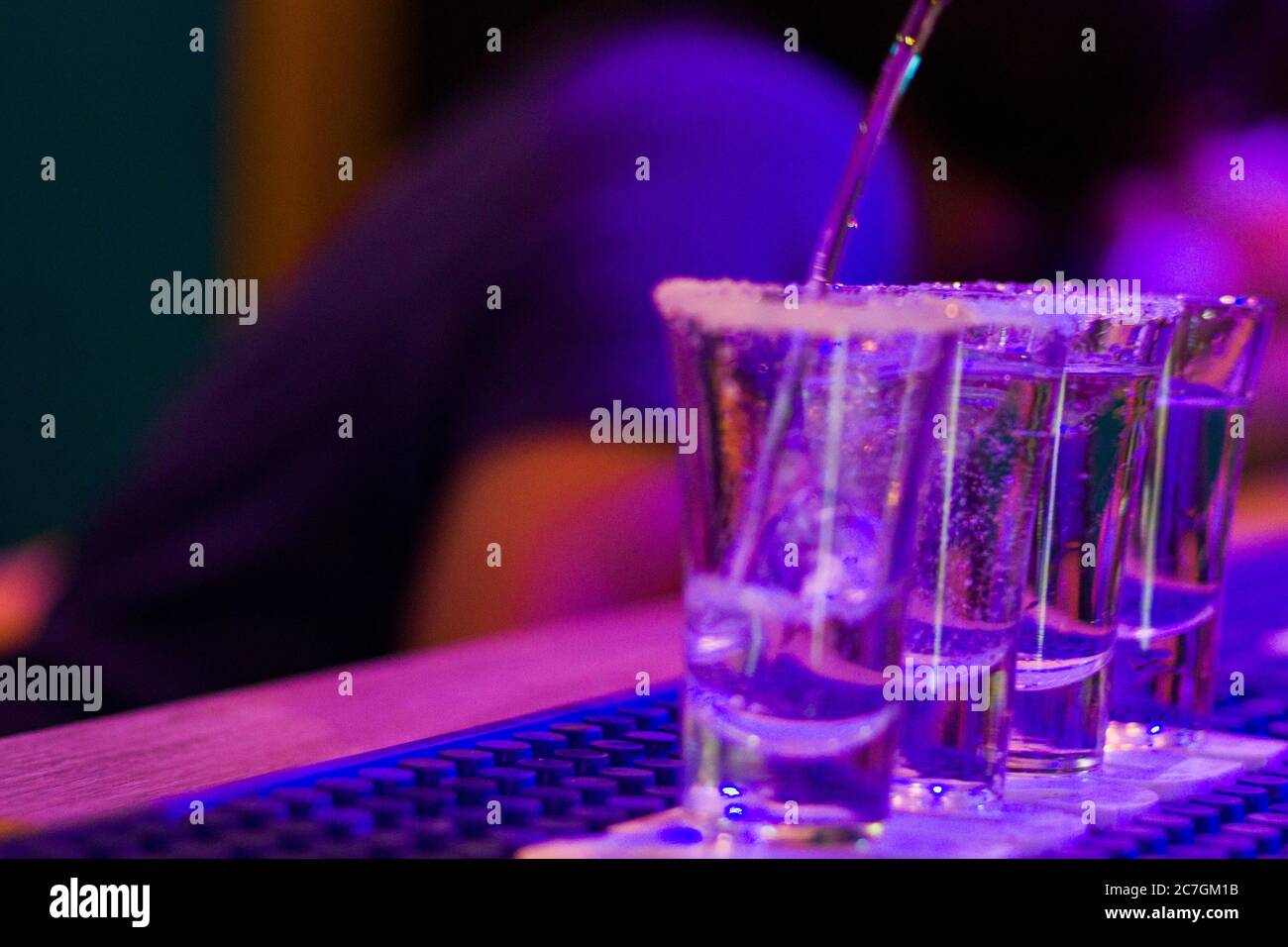 Tequila shots on the bar table at night party, people on the background ...