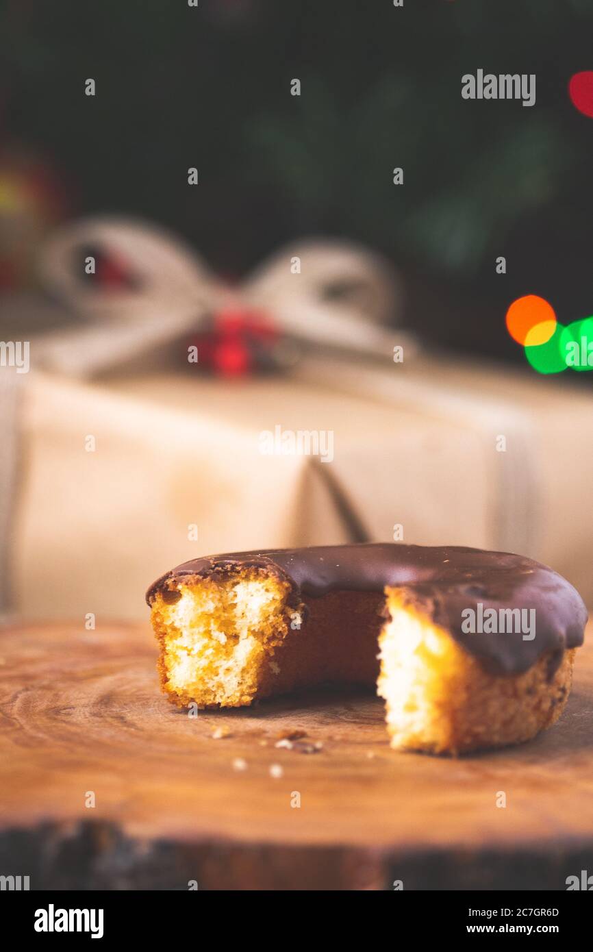 Vertical closeup of half bitten chocolate-dipped doughnut with a blurry ...
