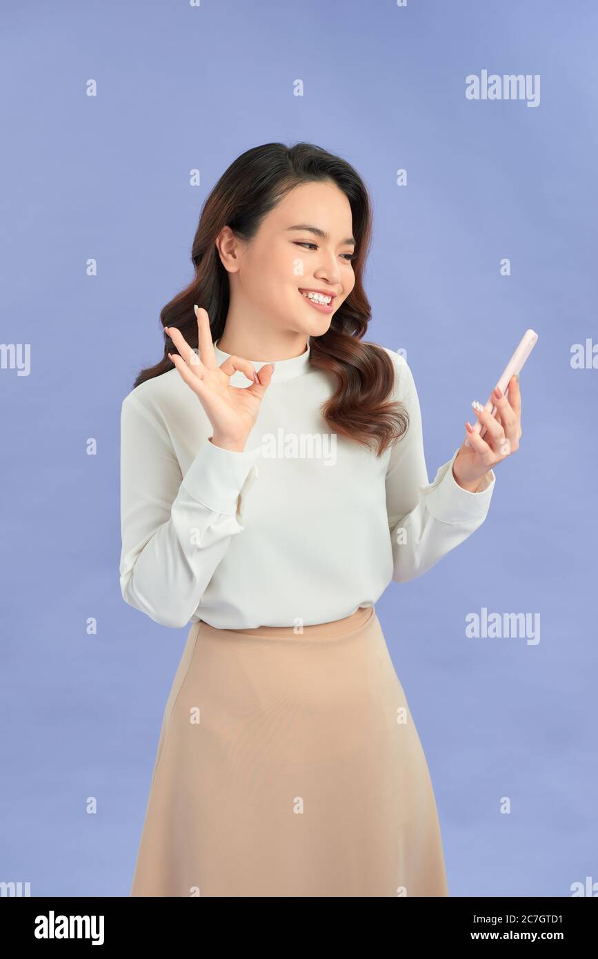 Young woman talking mobile over isolated purple background showing ok ...
