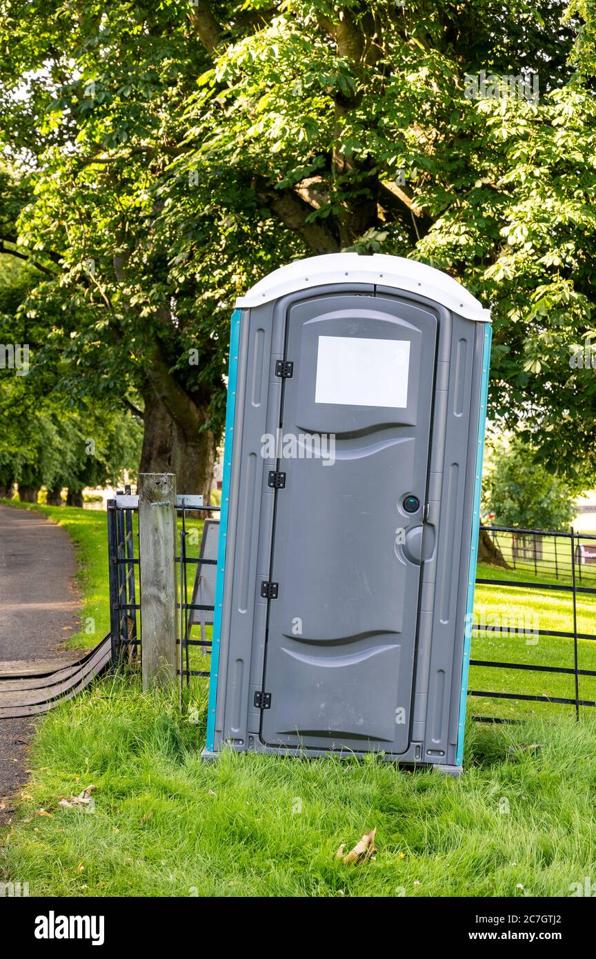A plastic portable toilet next to a fence in a field at an outdoor ...