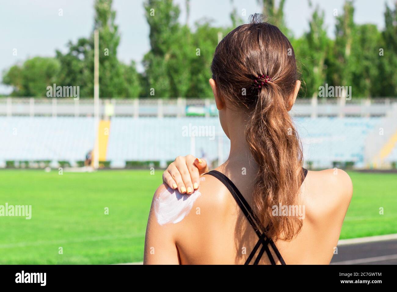 Fitness woman is applying sunscreen on her shoulder before training at ...