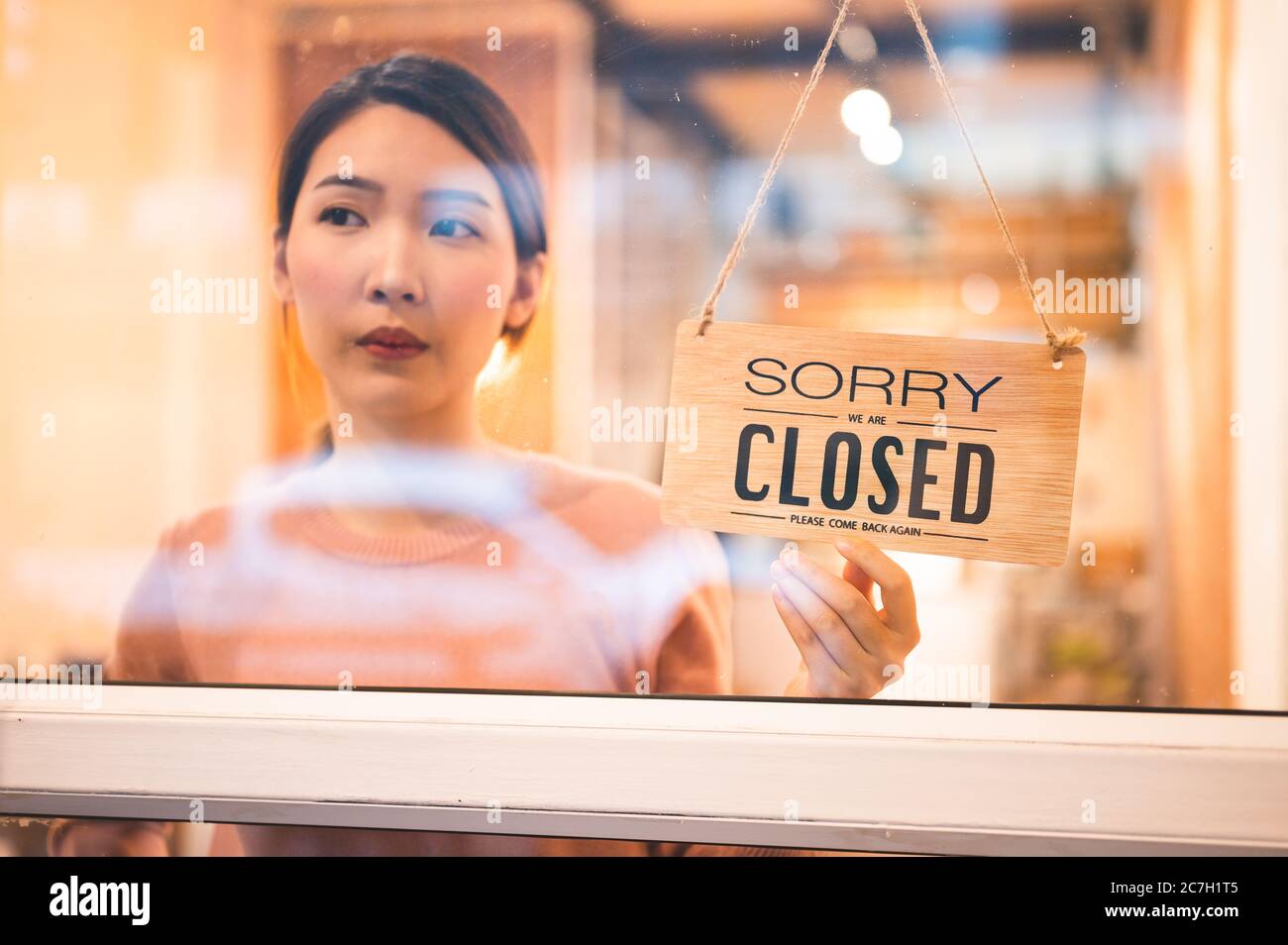 Asian woman store owner turning hanging closed sign in front door of ...