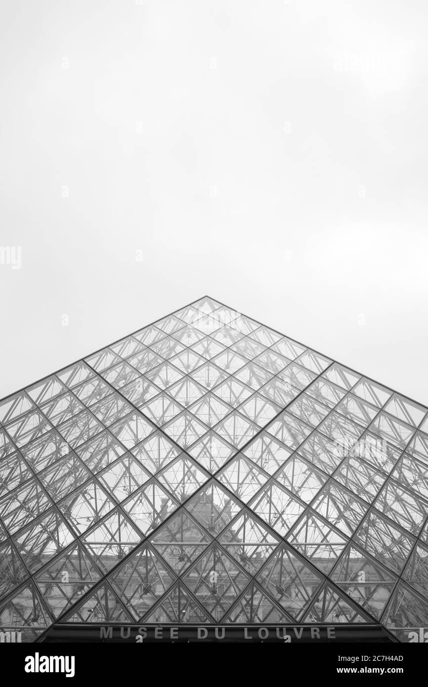 Low angle greyscale of the Louvre Museum under a cloudy sky in Paris in ...