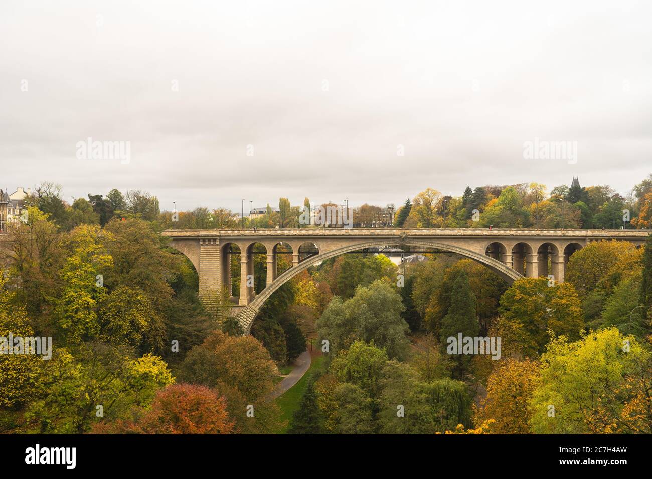 Arch bridge surrounded by trees under a cloudy sky during autumn Stock ...