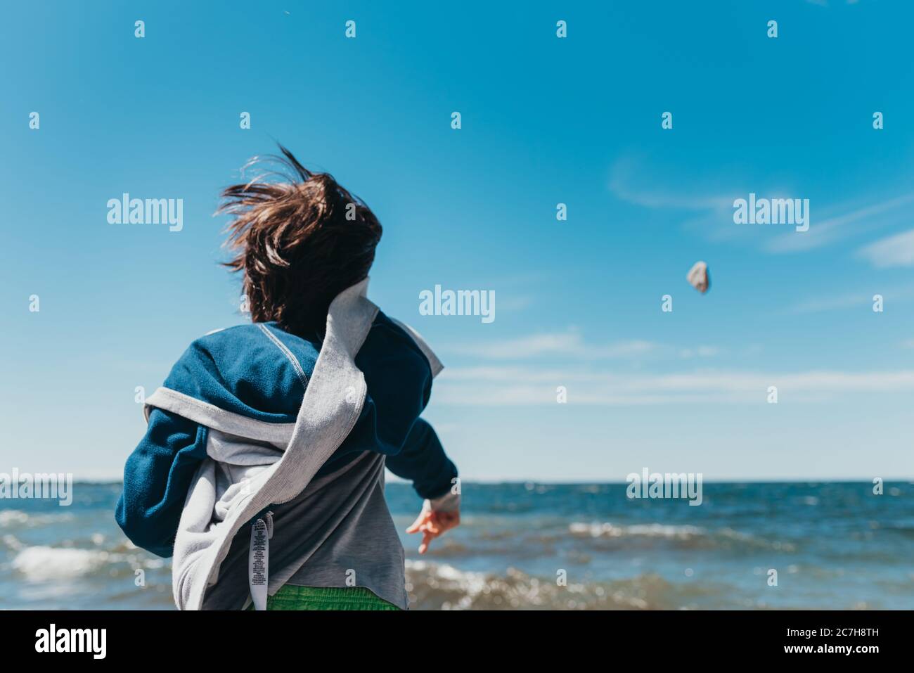 Back view of a boy throwing a rock into a lake on a windy day Stock ...