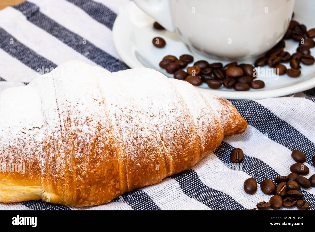 Puff pastry, coffee cup and buttered French croissant on wooden crate ...