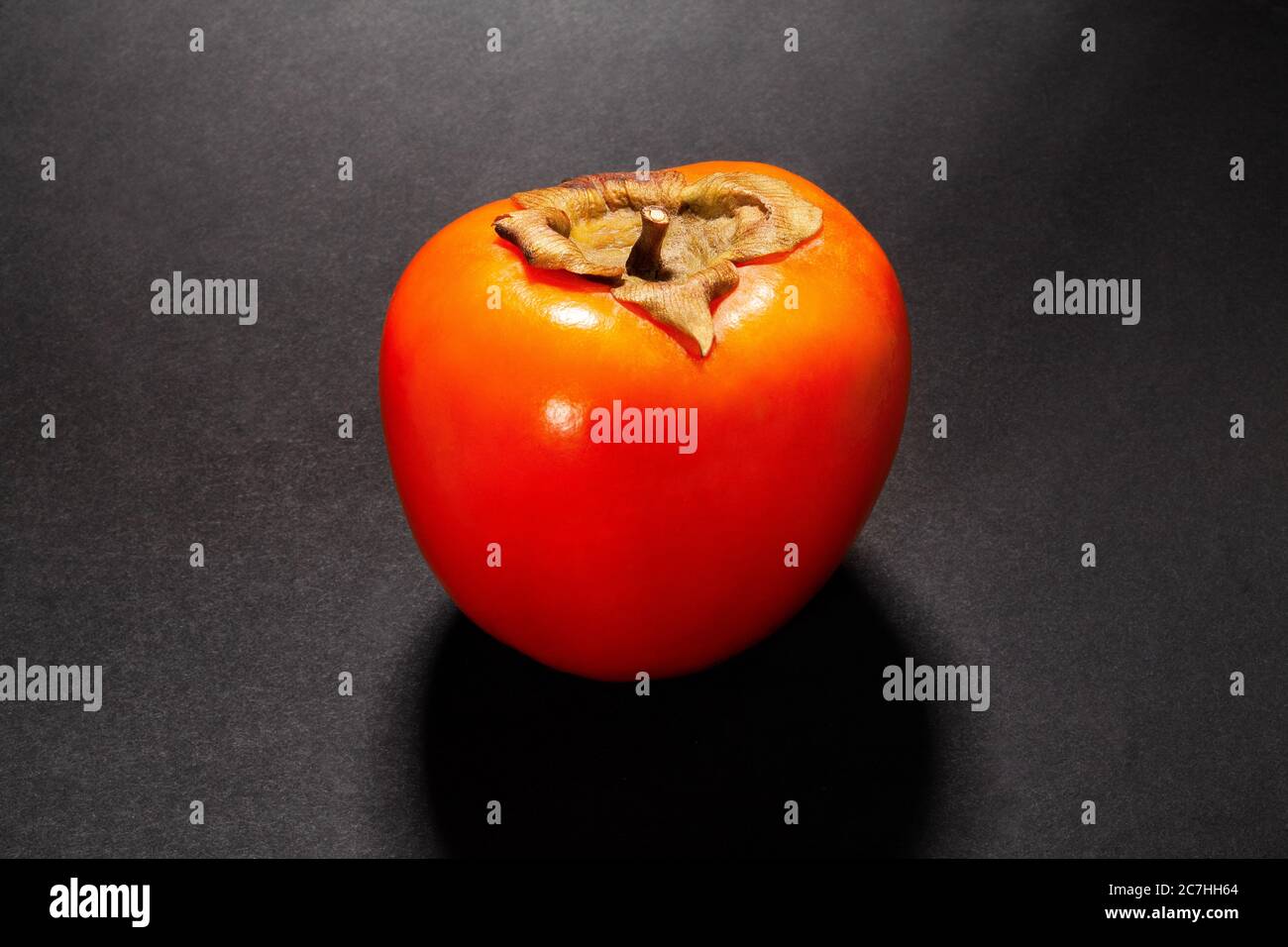 single persimmon on black background Stock Photo - Alamy
