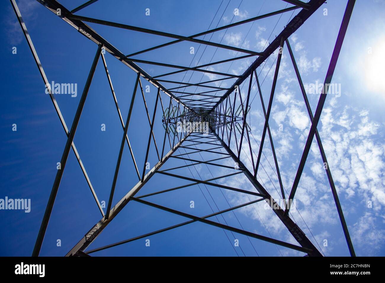 Low angle view of an overhead power line under a blue sky and sunlight ...