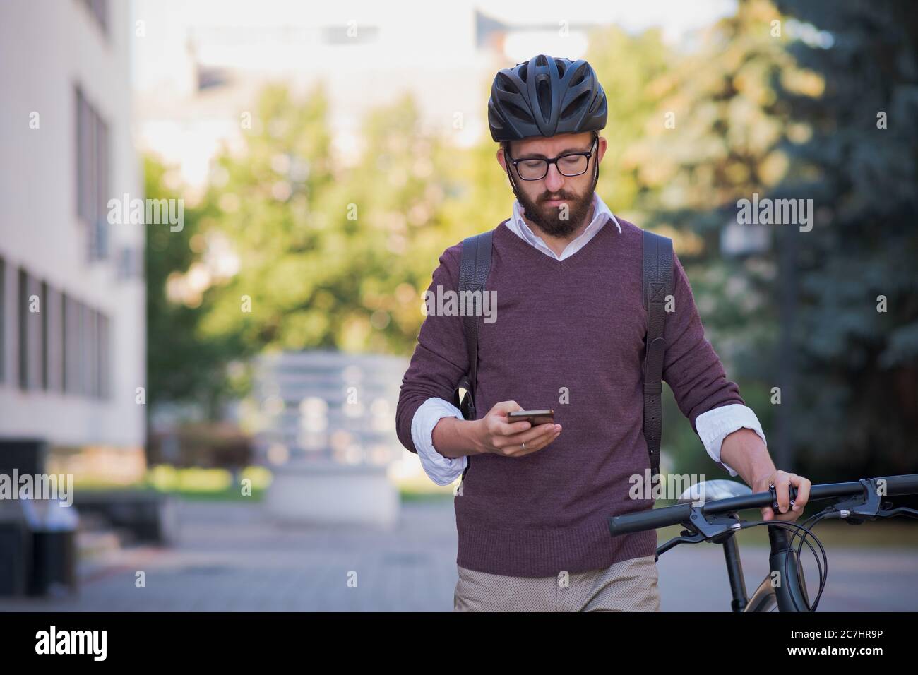 Millennial bike commuter in helmet walks with a phone. Safe cycling in ...