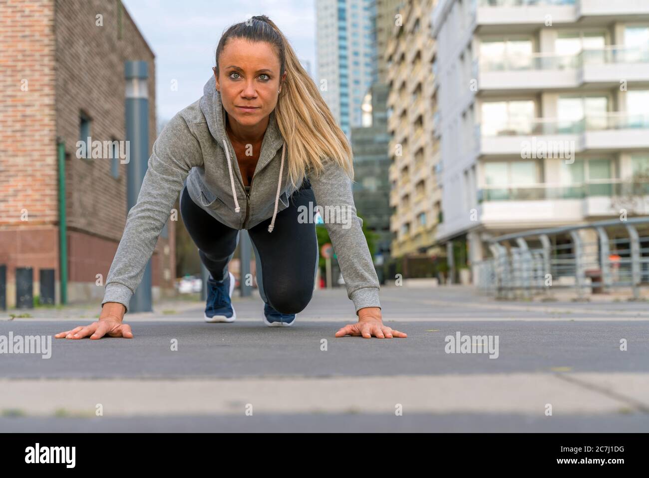 An athletic woman stretching in a grey sweater stretching on the street ...