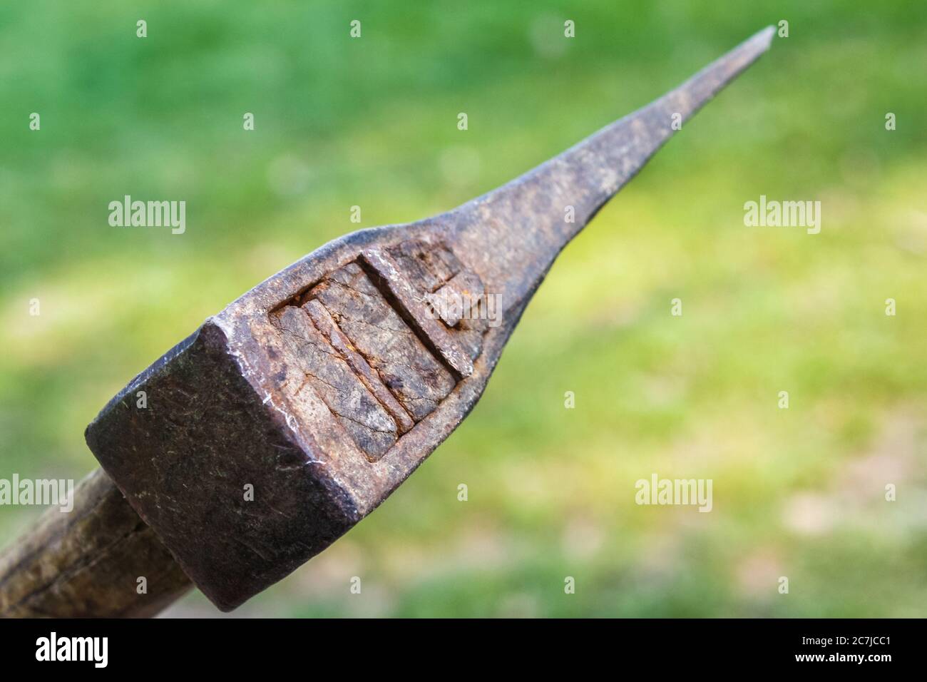 Closeup of an old rusty axe under sunlight with greenery on the blurry ...