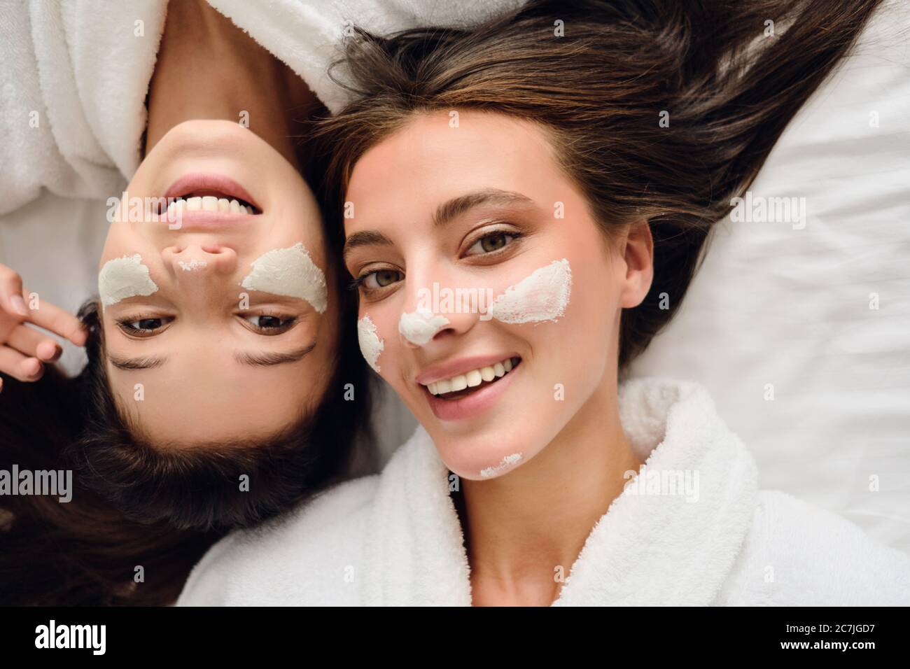 Two Young Gorgeous Women With Dark Hair In White Bathrobes Lying Near